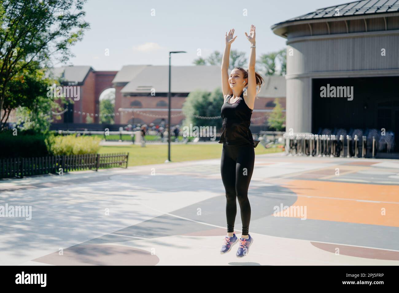 Positive active female model has cardio training outdoors jumps high ...