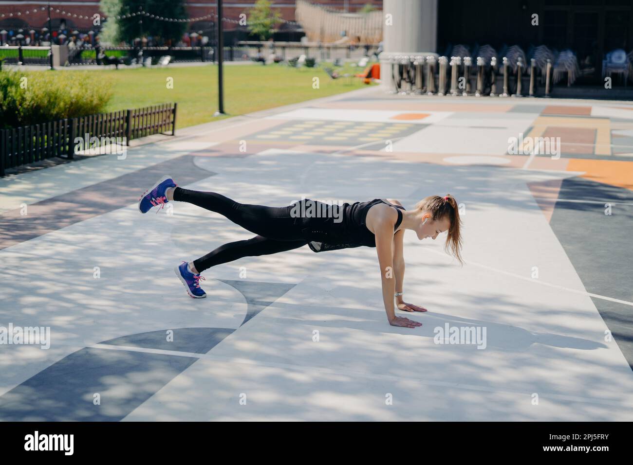 Sporty slim young woman does planking exercise raises leg demonstrates ...