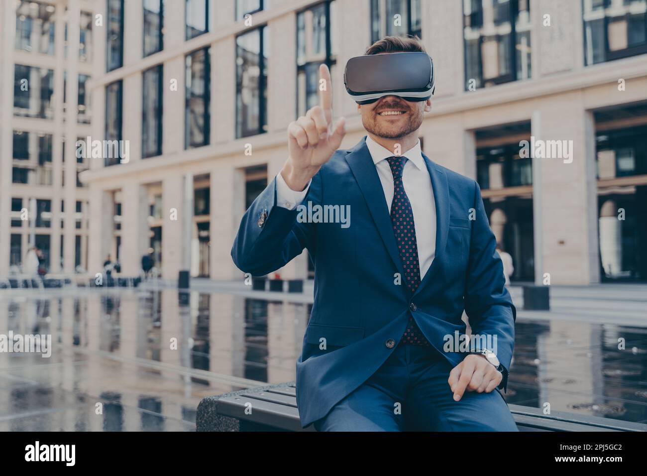 Happy young businessman in blue suit using virtual reality goggles ...
