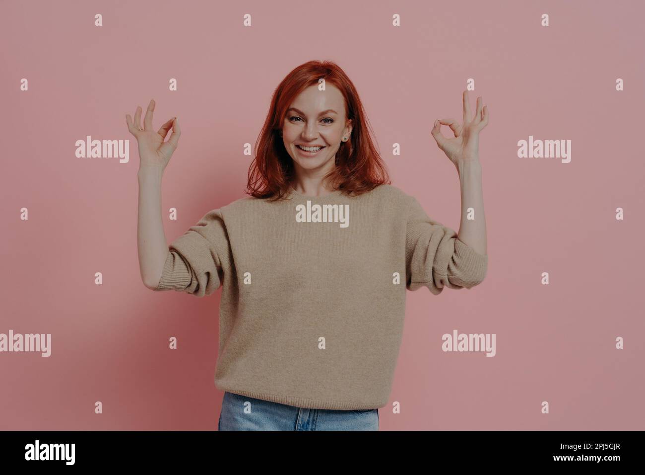 Half length shot of pretty ginger woman showing OK sign with both hands ...