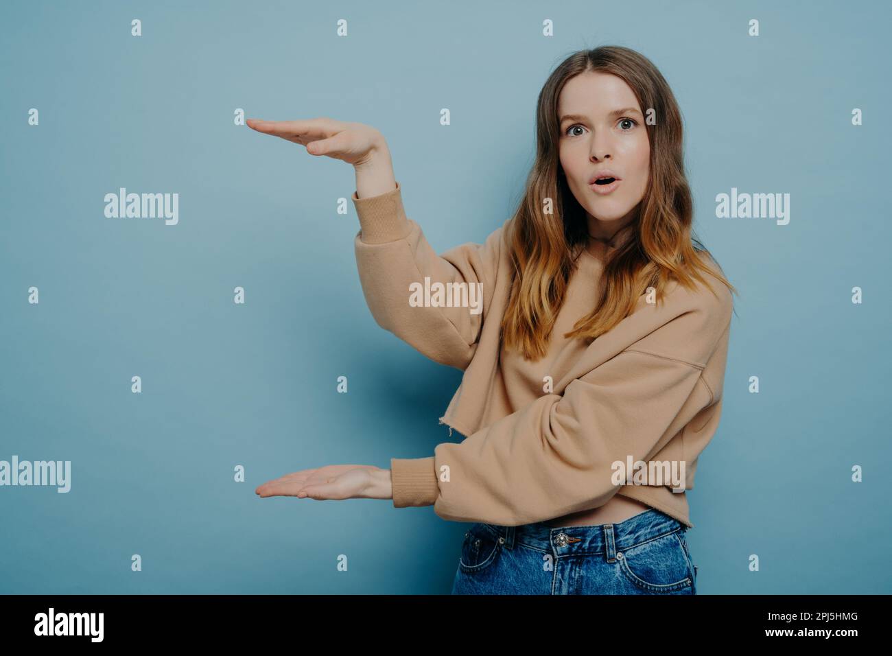 Surprised young woman wearing casual clothes presenting size of product ...
