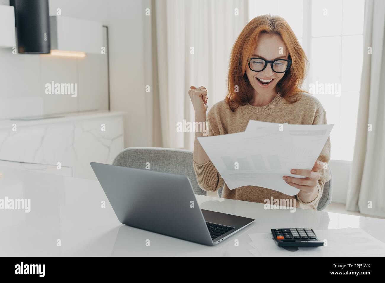 Successful ginger female freelancer checks calculations clenches fist ...