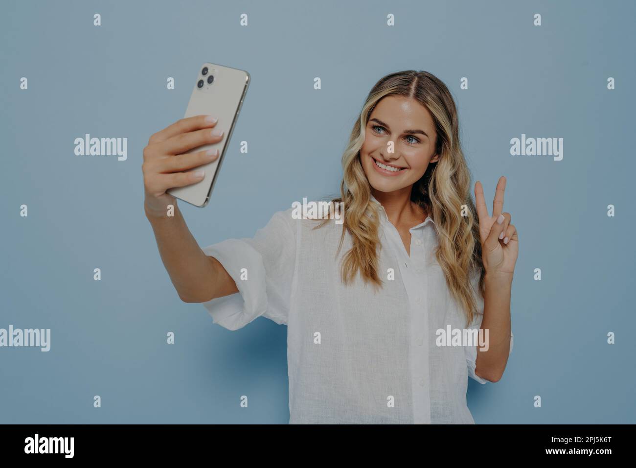 Young happy woman in casual clothes taking selfie while showing peace ...