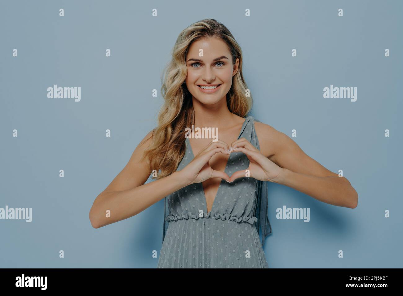 Smiling blonde romantic female showing heart gesture with her hands ...