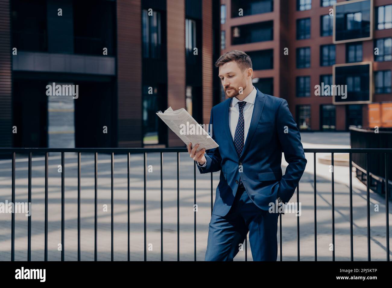 Handsome male boss wearing blue suit, reading newspaper thoughtfully ...