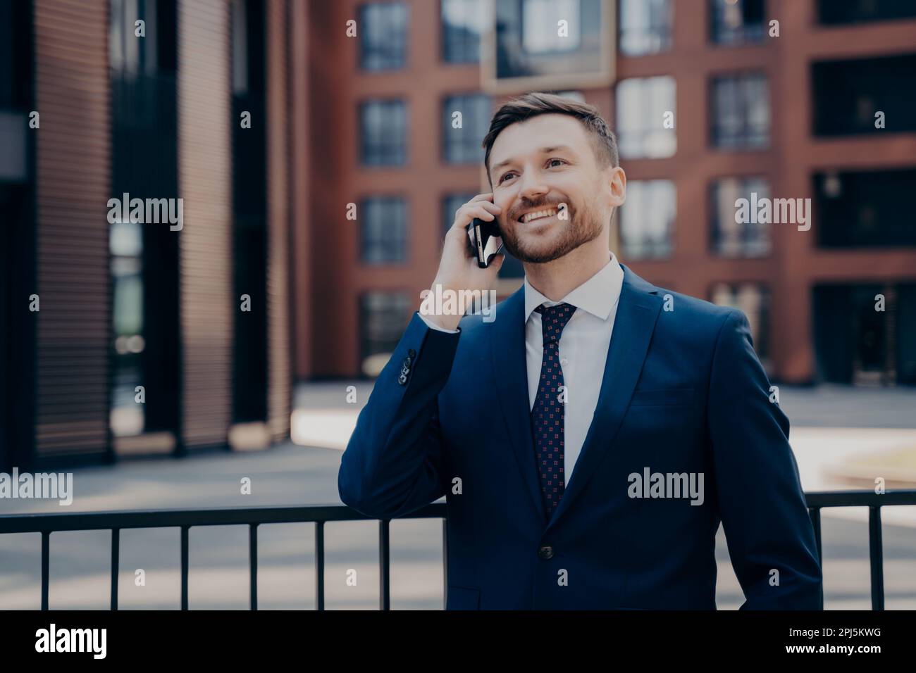Happy male office worker in blue suit talking on phone with colleague ...