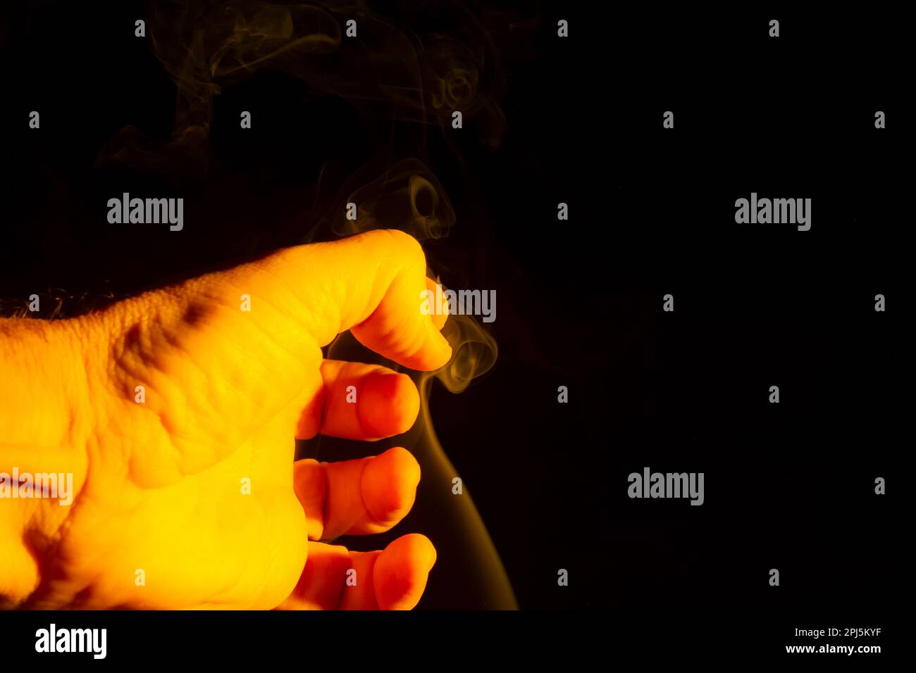 A male hand lit yellow with smoke around it isolated on a black ...