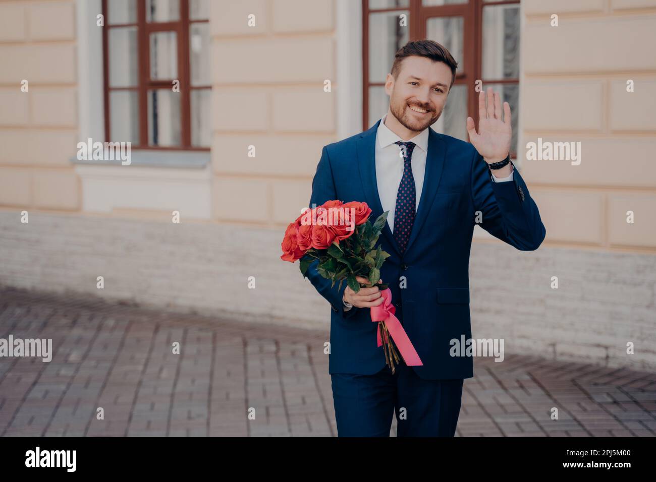 Formally dressed happy young man in blue suit waving with hand to his ...