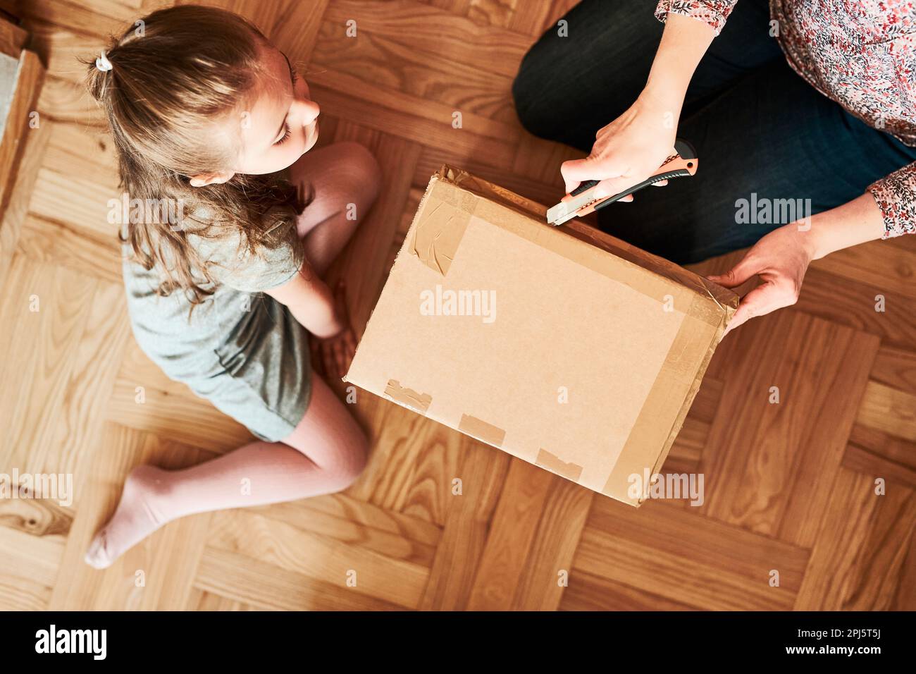 Woman unpacking a cardboard box parcel in room at home. Little girl ...