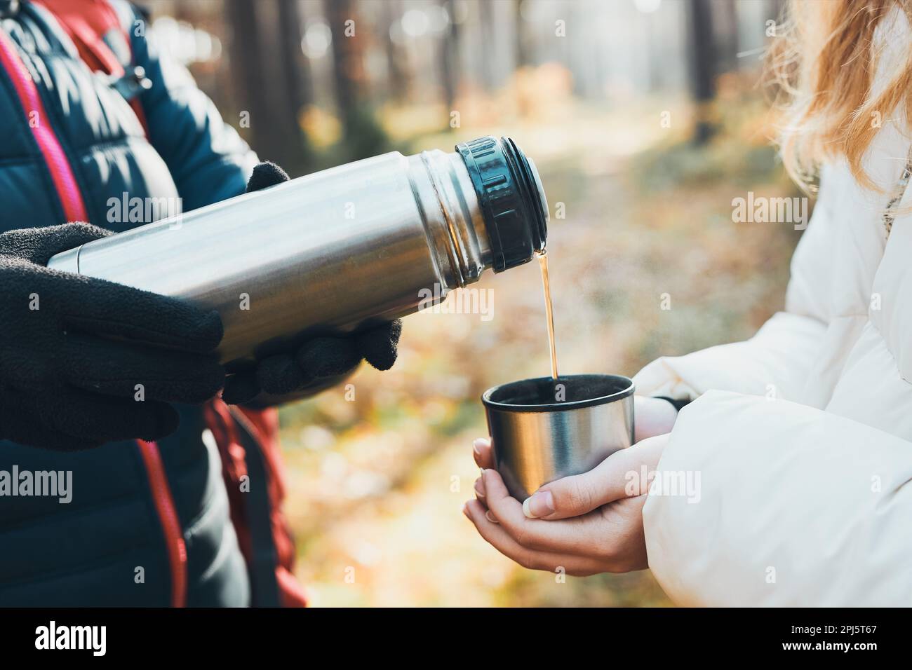 Women having break during autumn trip pouring a hot drink from thermos ...