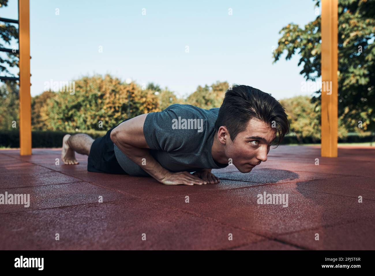 Young man doing push-ups on a red rubber ground during his workout in a ...