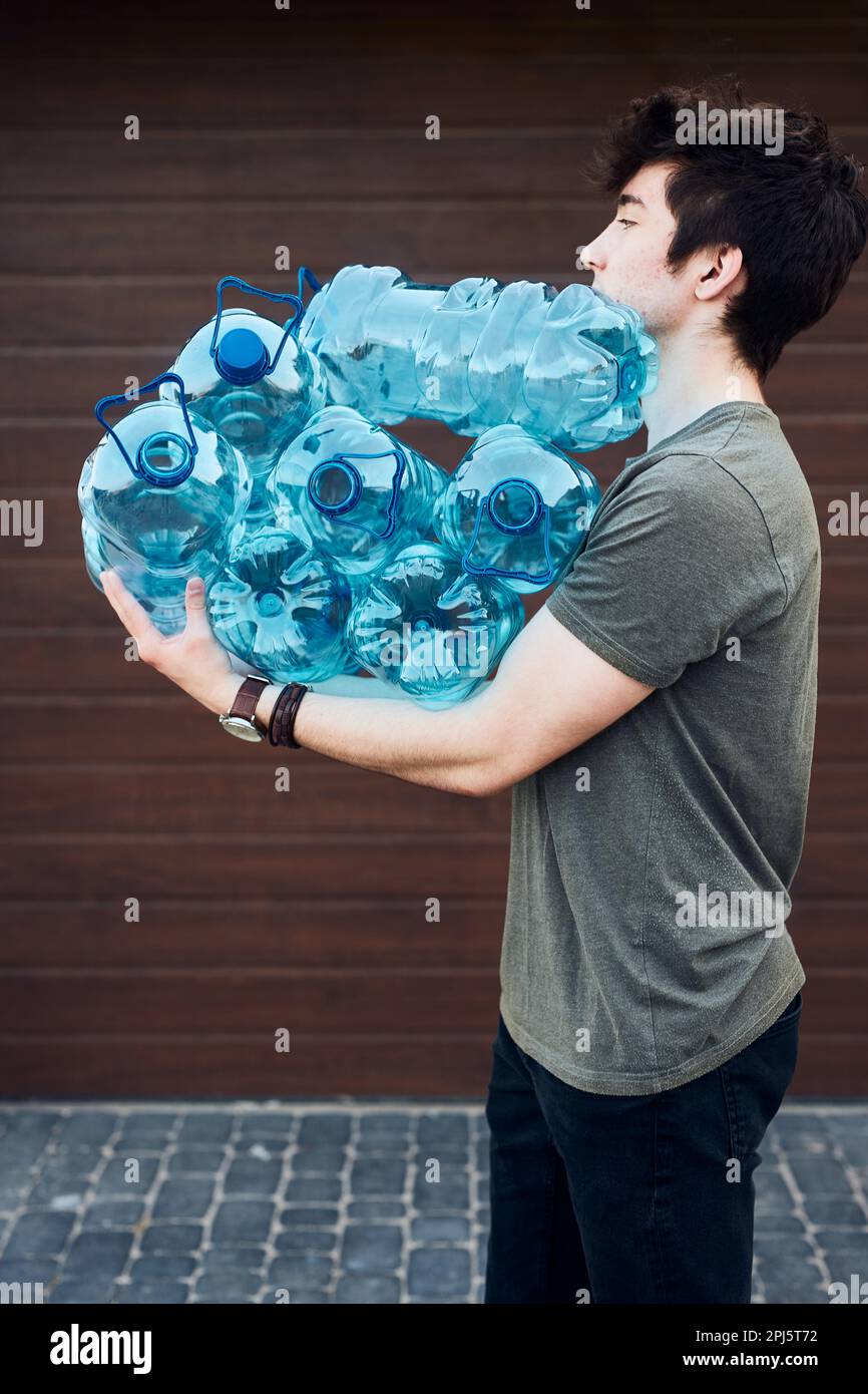 Young man throwing out empty used plastic water bottles into trash bin ...