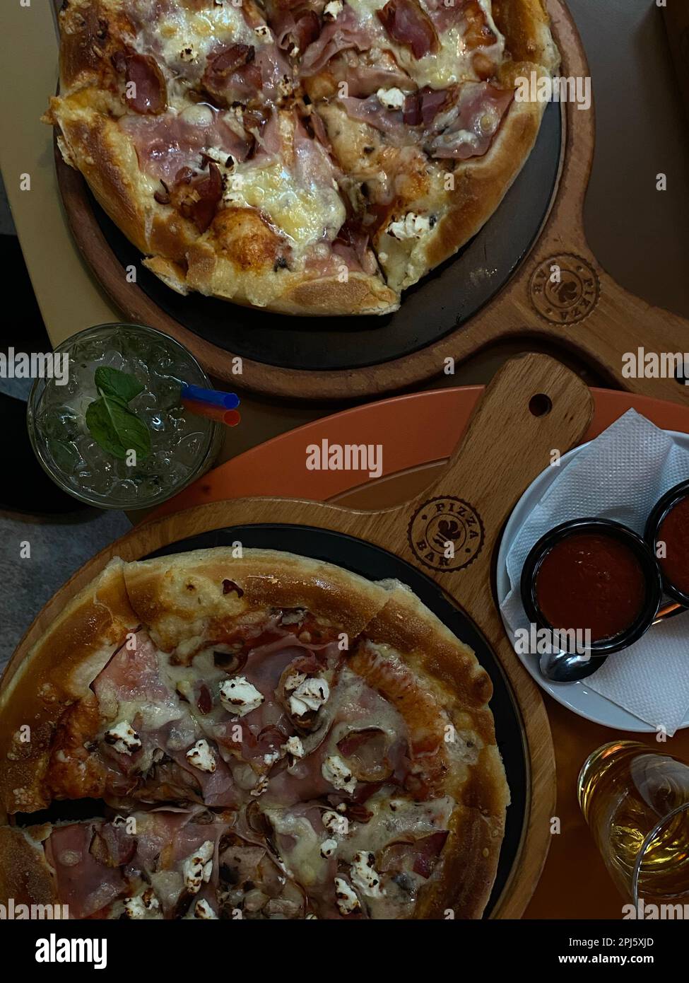Two pizzas are presented on wooden boards, with a variety of toppings ...