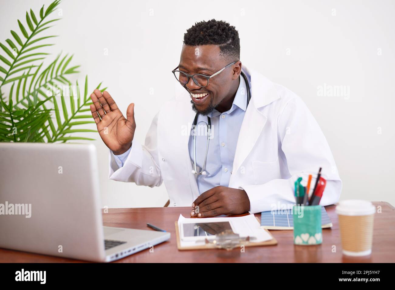 Happy friendly doctor waves hello to patient on telehealth call, remote ...