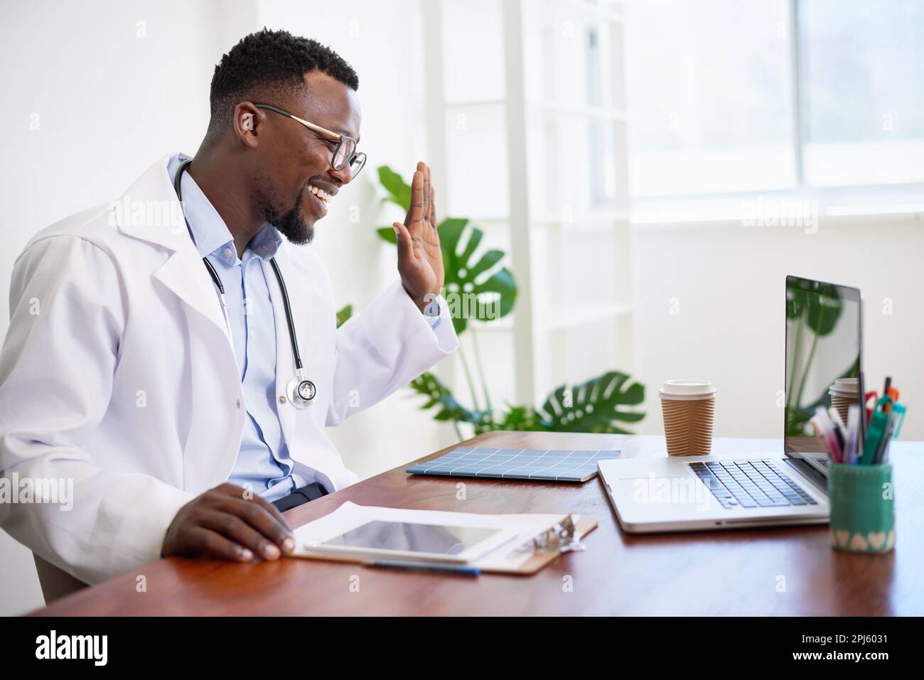 Happy friendly doctor waves hello to patient on telehealth call, remote ...