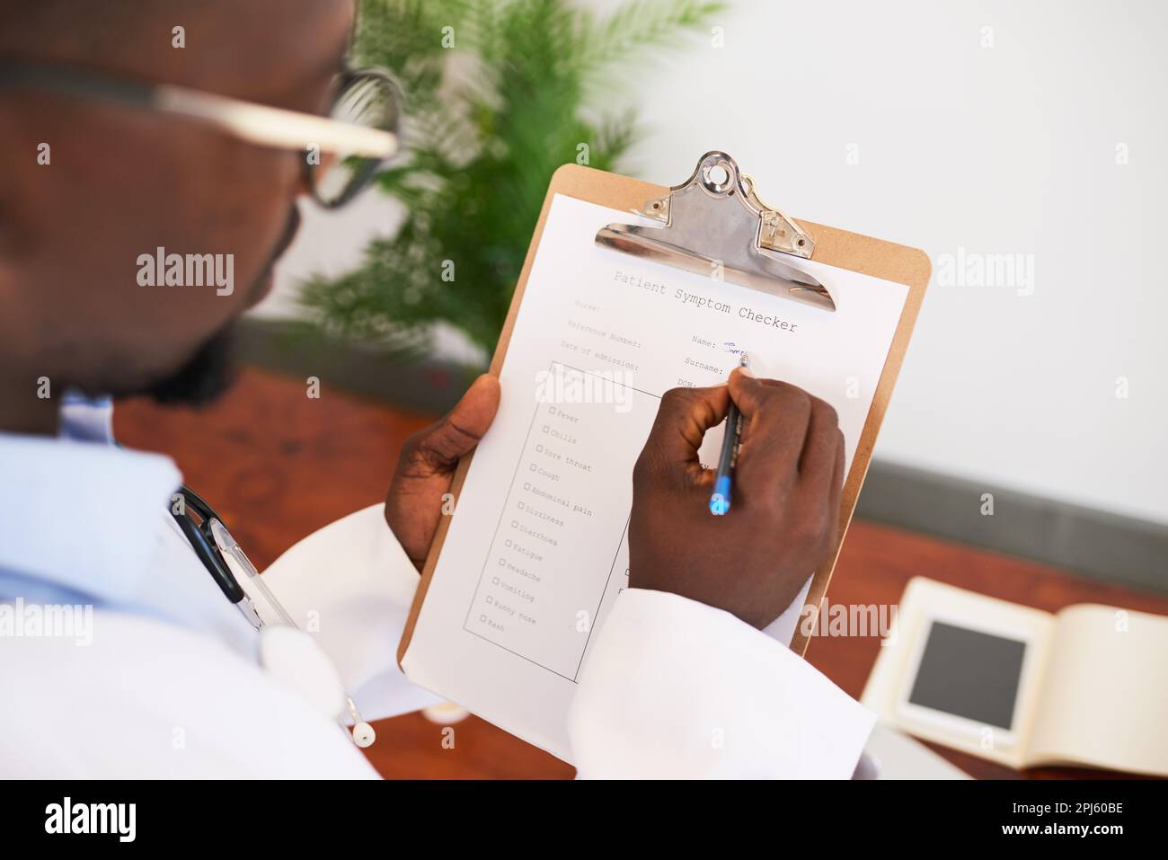 Over the shoulder shot of doctor filling in patient symptom checklist ...