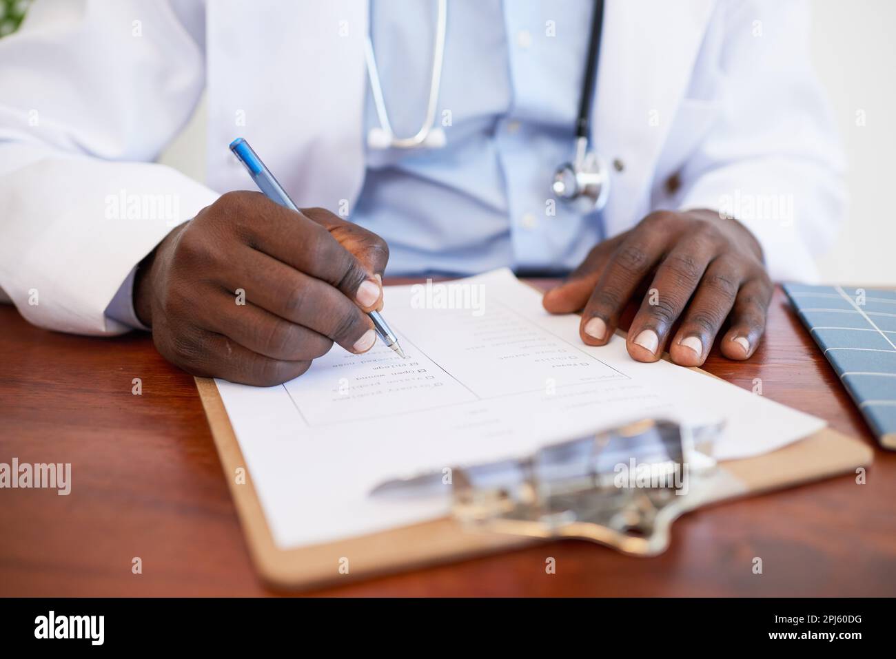 Close up shot of Black doctor filling in patient symptoms on clipboard ...