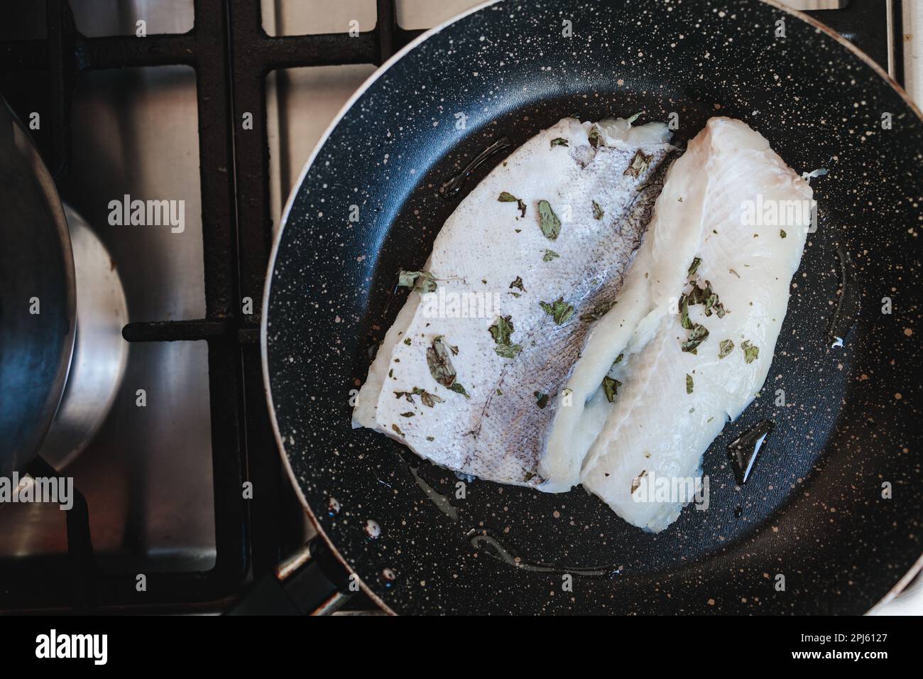 cooking fried hake fish in a frying pan, on a metal grill with red hot ...