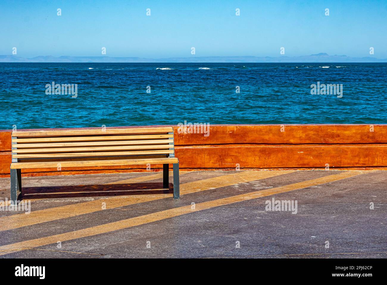 Empty wooden bench on the coastal boardwalk, sea in background against ...