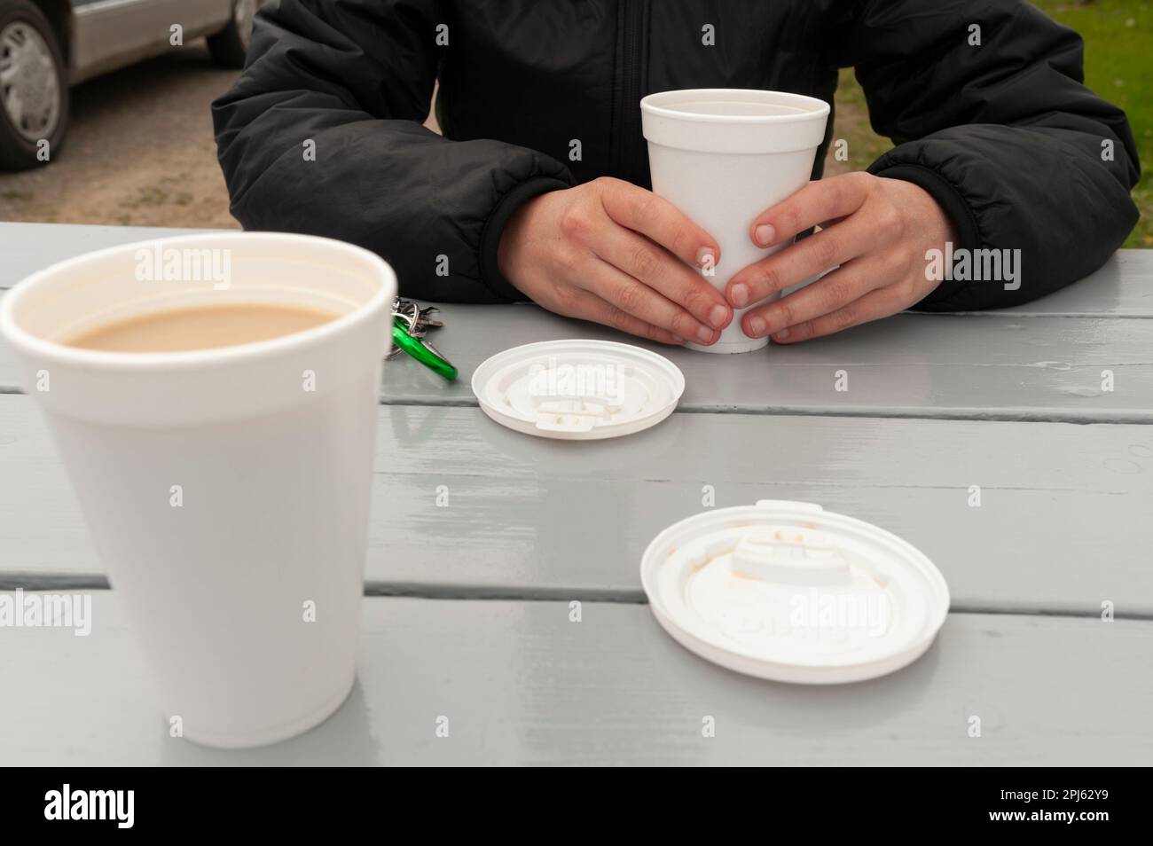 A young woman's hands hold a coffee cup, with keys on a picnic table ...