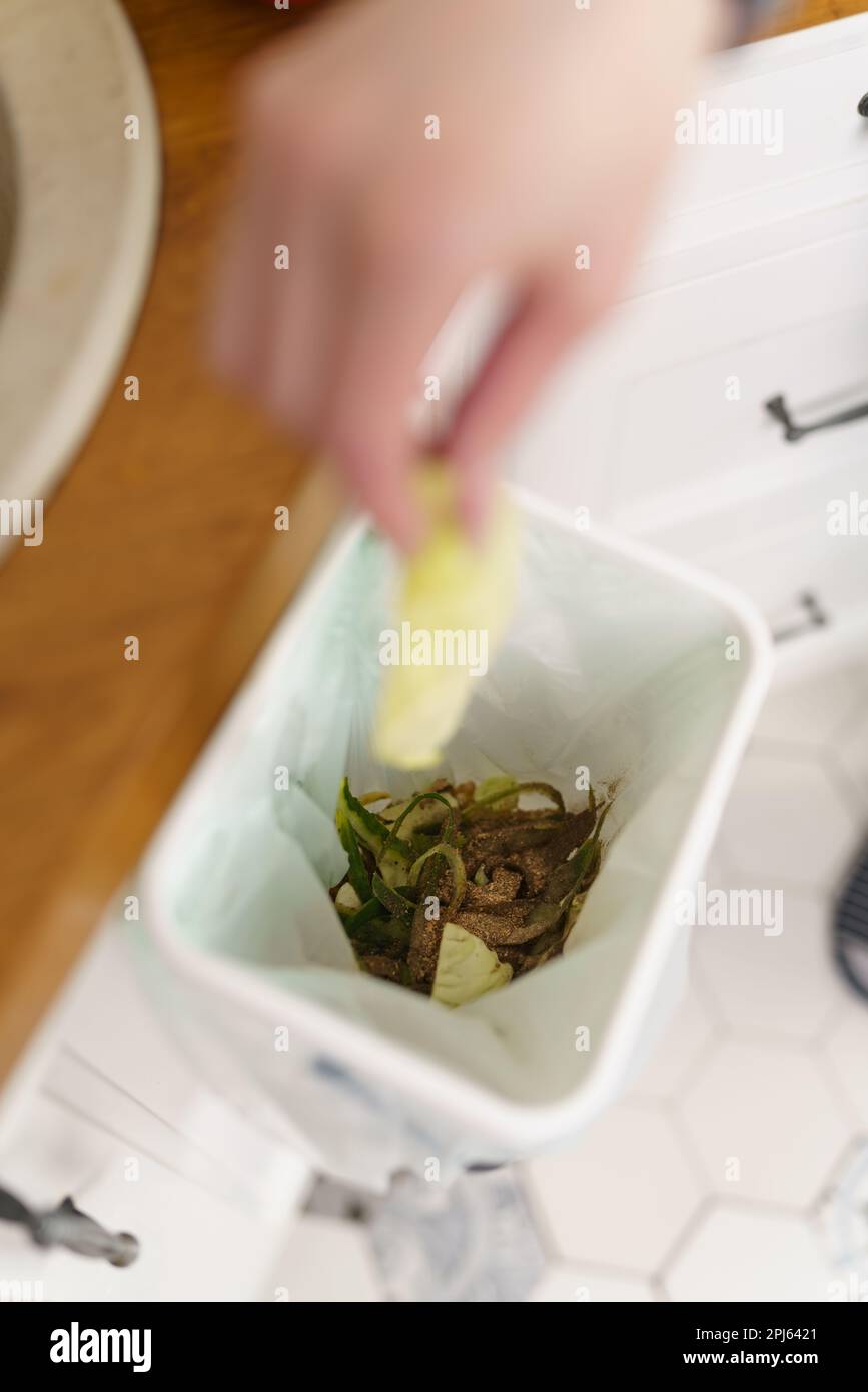 Female hand throwing vegetable peel in a compost bin in a home kitchen ...