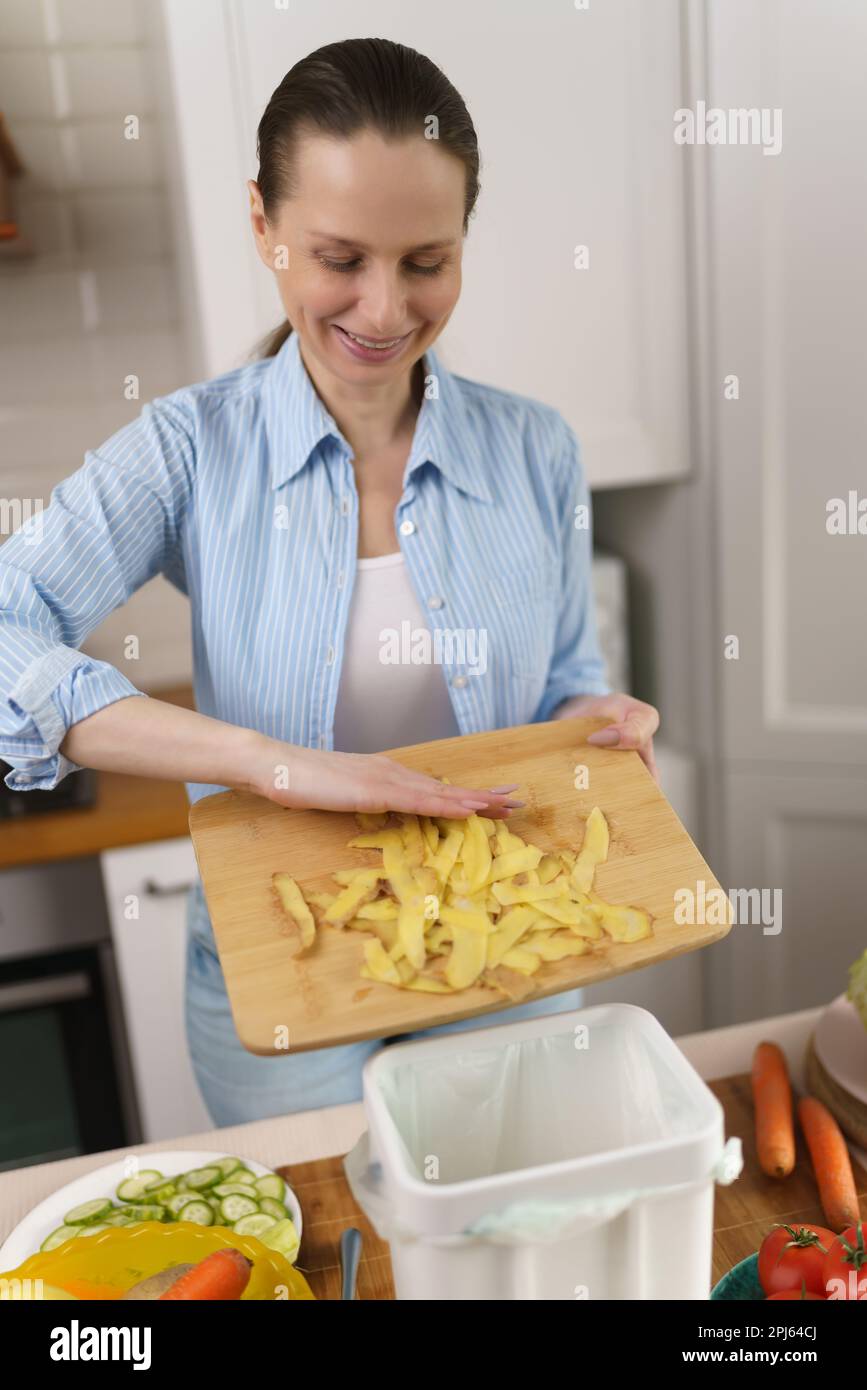 Cheerful adult woman recycling compostable food leftovers in a bin ...