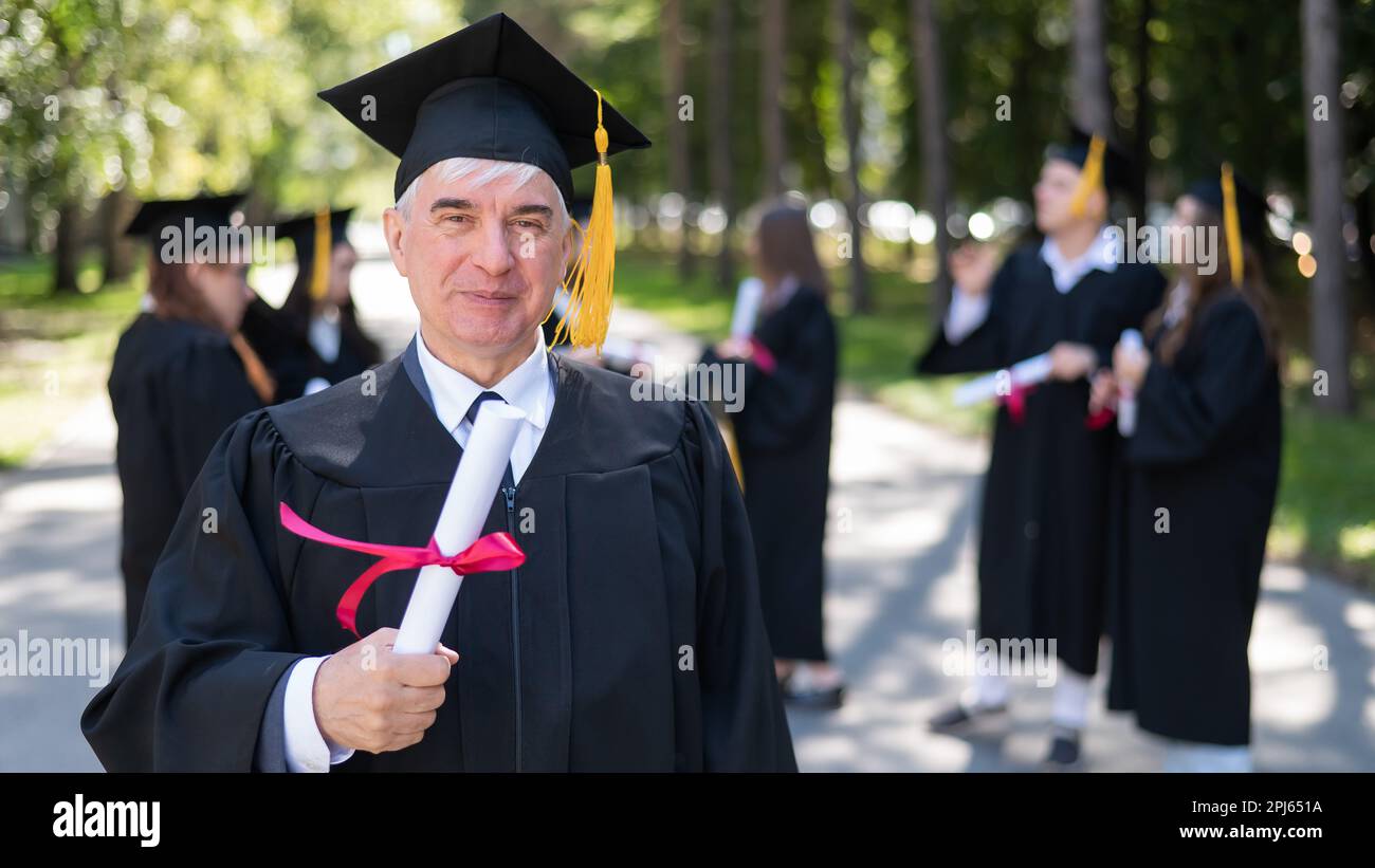 A group of graduates in robes outdoors. An elderly student rejoices at ...