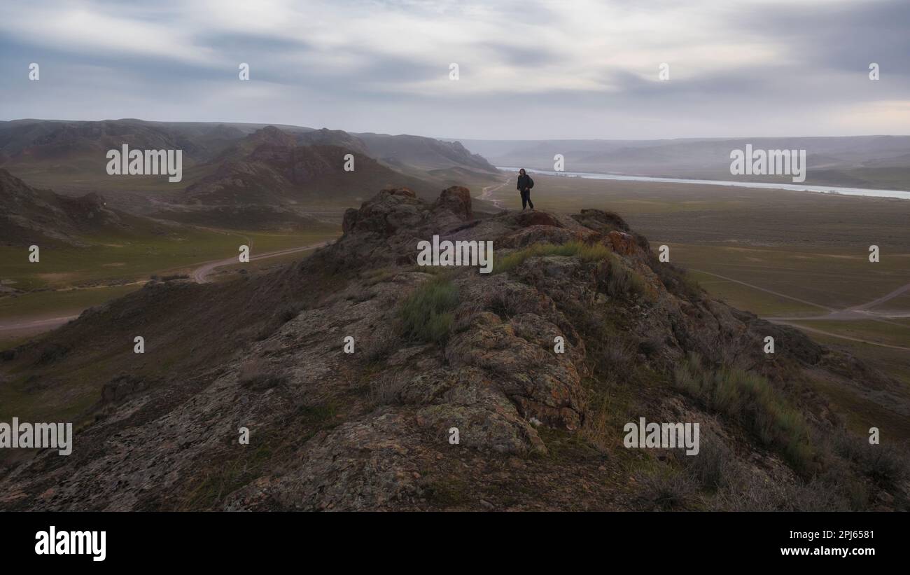a man on a rock overlooking the rivers and the valley in windy gloomy ...