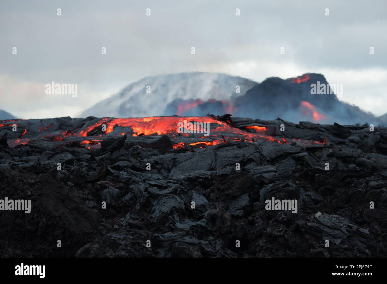 A volcanic eruption with glowing orange lava flow surrounded by a pool ...