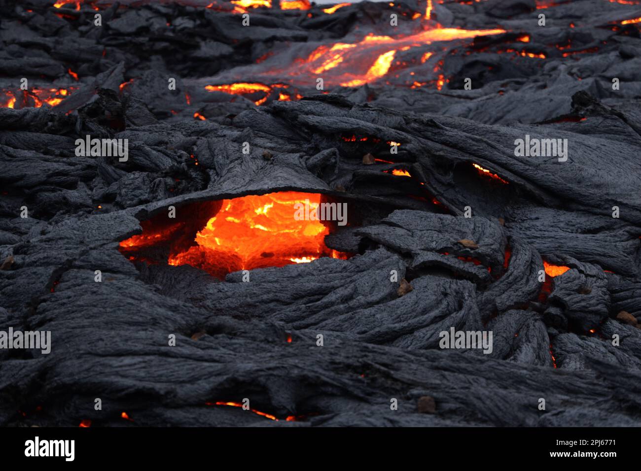 A volcanic eruption with glowing orange lava flow surrounded by a pool ...