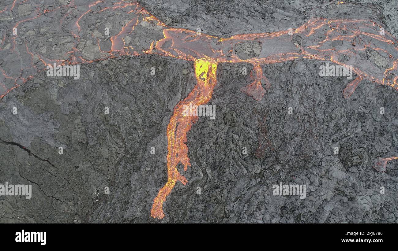 A volcanic eruption with glowing orange lava flow surrounded by a pool ...