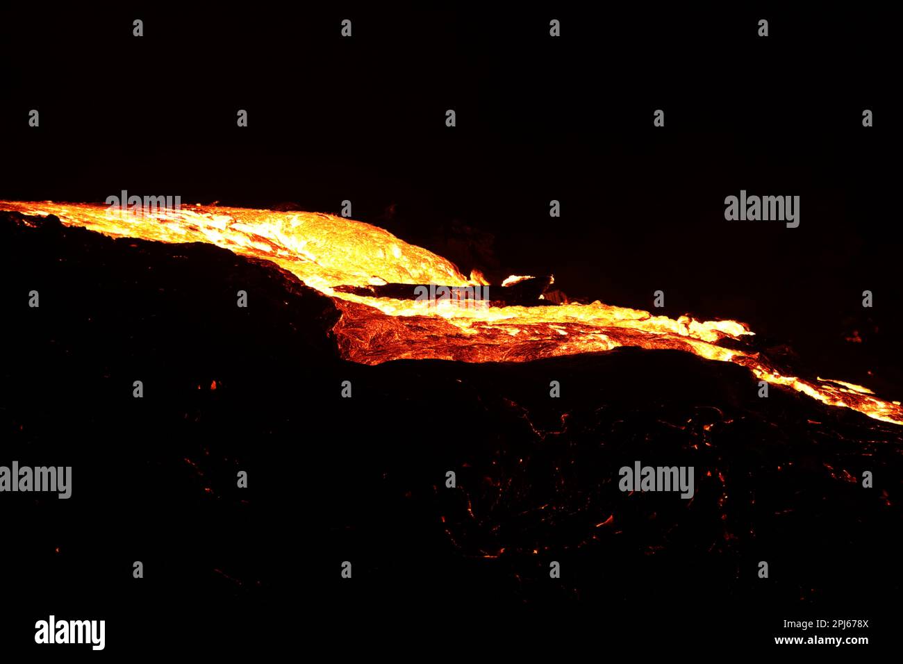 A volcanic eruption with glowing orange lava flow surrounded by a pool ...