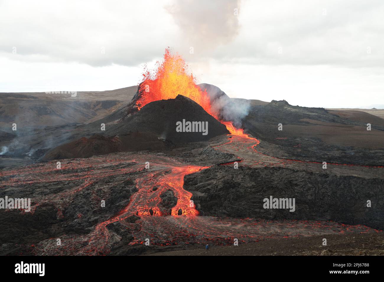 A volcanic eruption with glowing orange lava flow surrounded by a pool ...