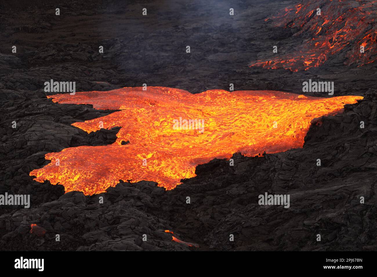 A volcanic eruption with glowing orange lava flow surrounded by a pool ...