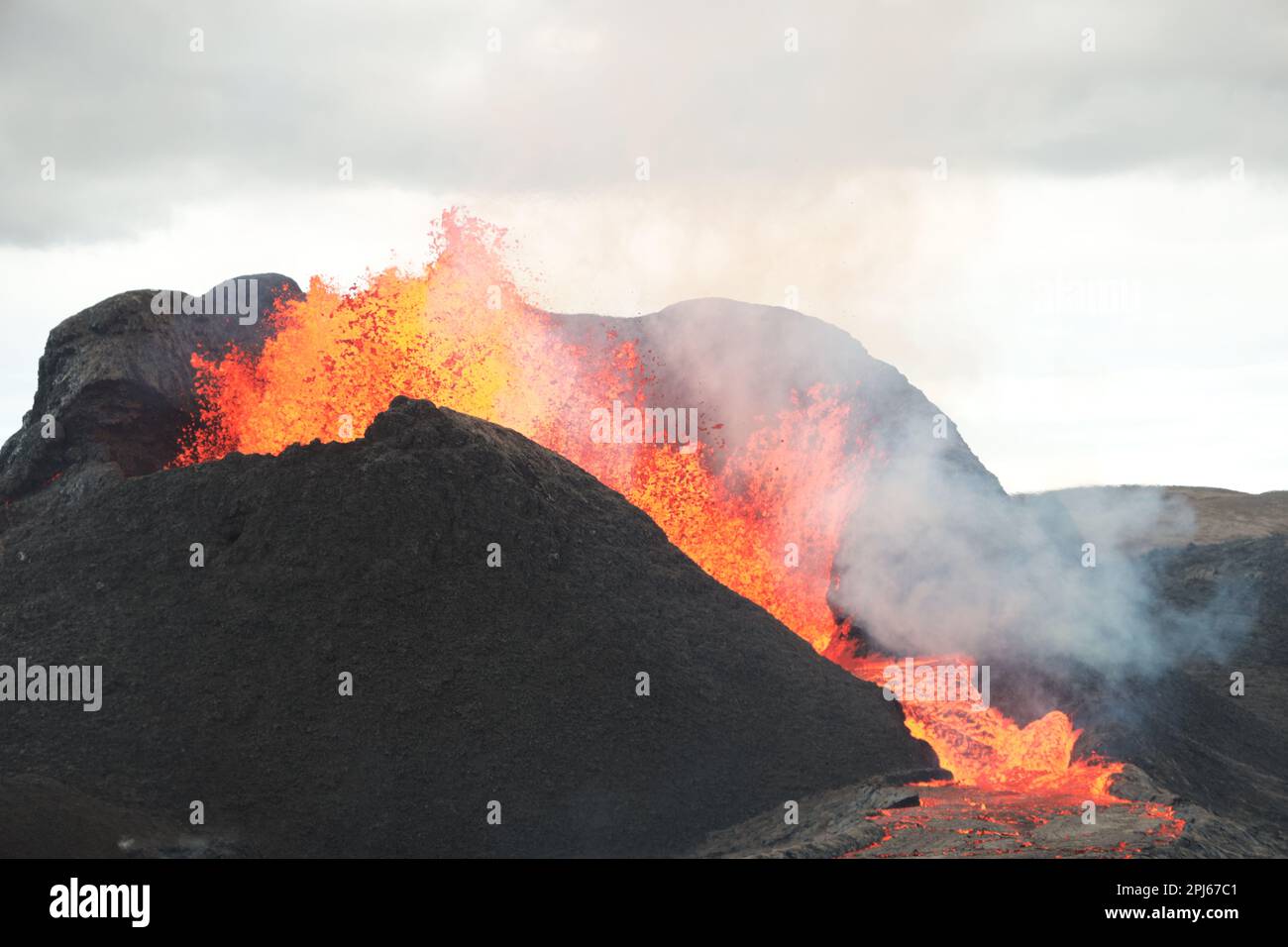 A volcanic eruption with glowing orange lava flow surrounded by a pool ...