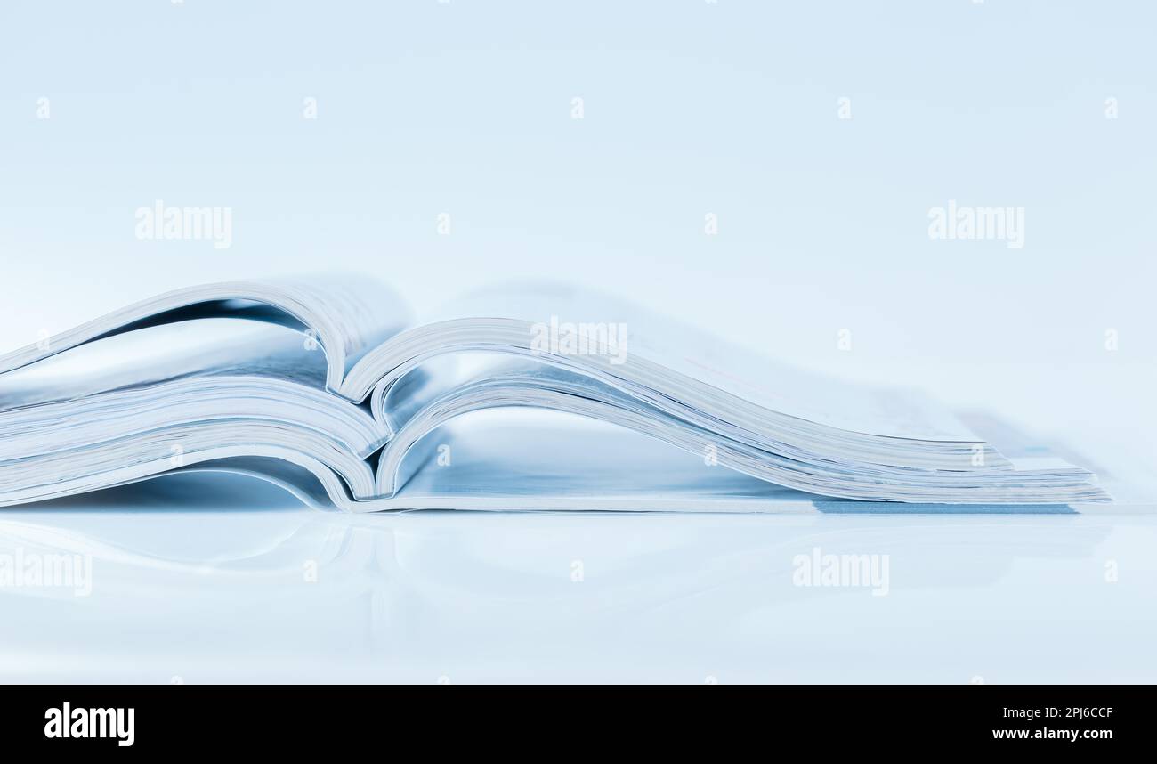 Stack of open magazines in blue tone on white background with copy ...