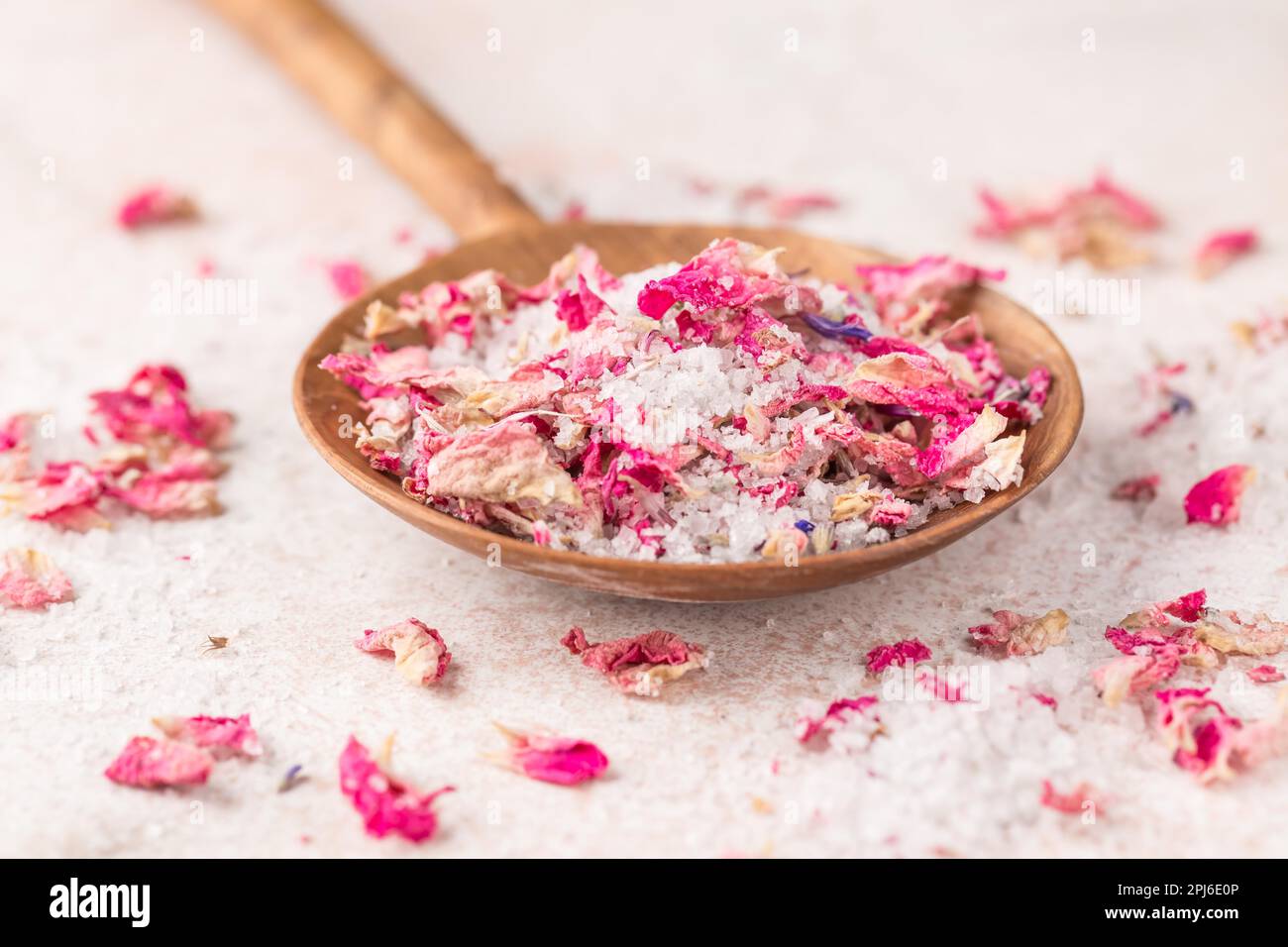 See salt wih with dried flower petals in wooden scoop on pink marble ...