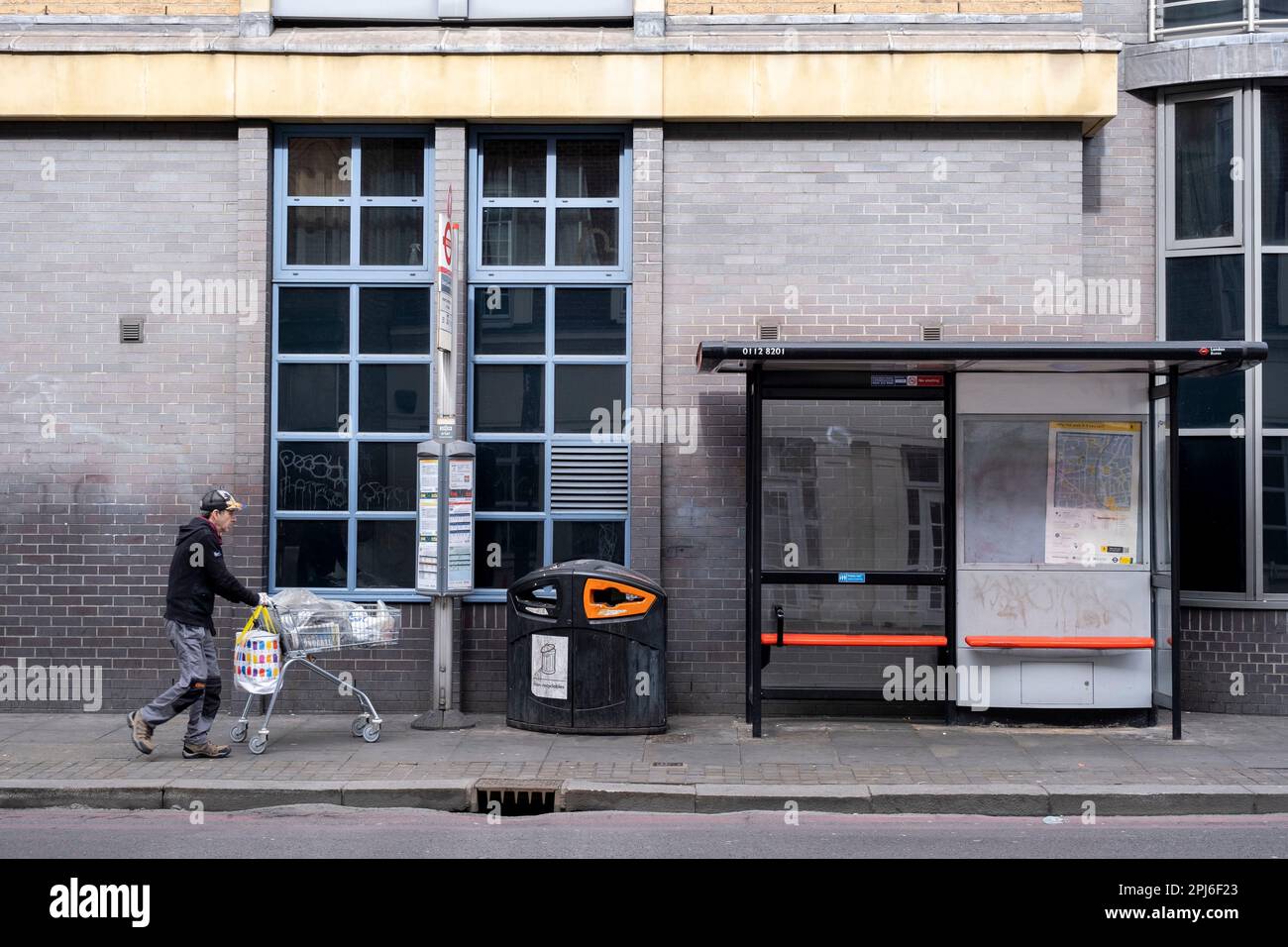 Man pushing a shopping trolley past a bus stop in Hoxton on 6th March ...