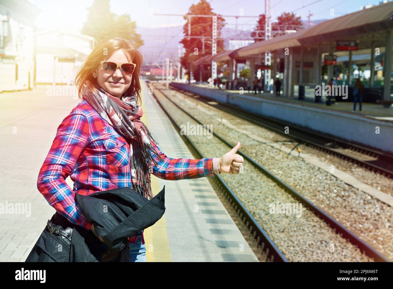 Woman tourist with jacket thumbs up waiting train on the railroad ...