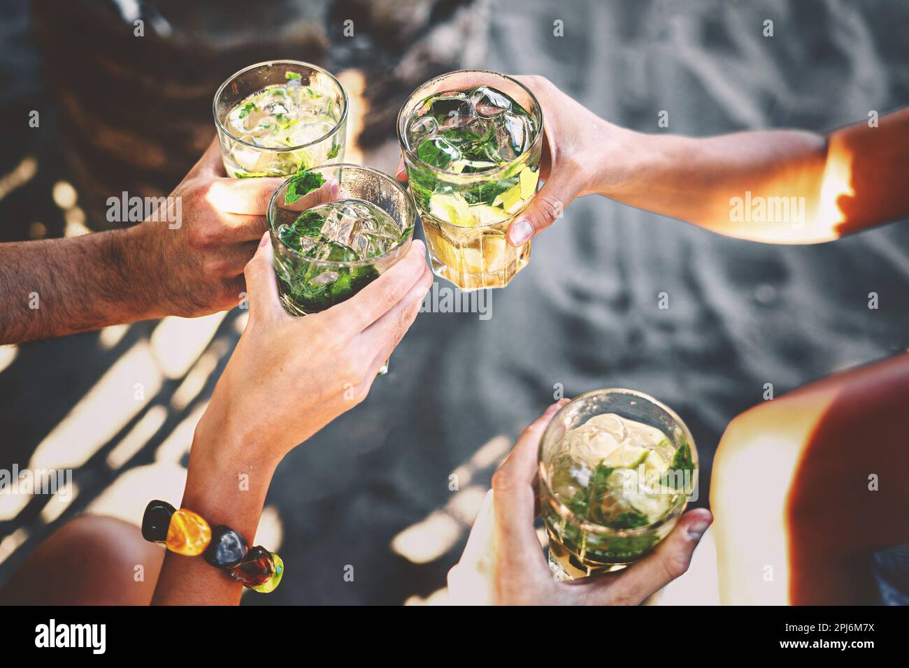 Four friends toasting with mojito glasses while sitting at a beach bar ...