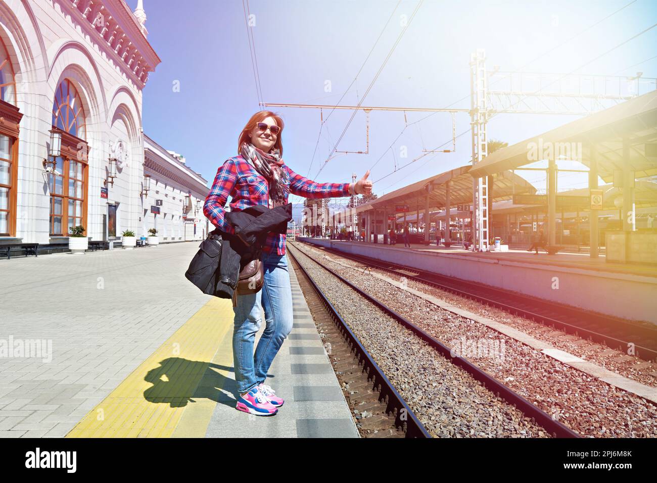 Woman tourist with jacket thumbs up waiting train on the railroad ...