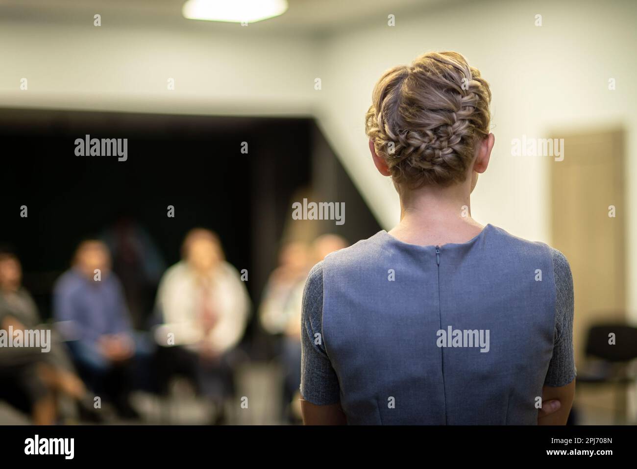 A woman stands in front of an audience.View from the back Stock Photo ...