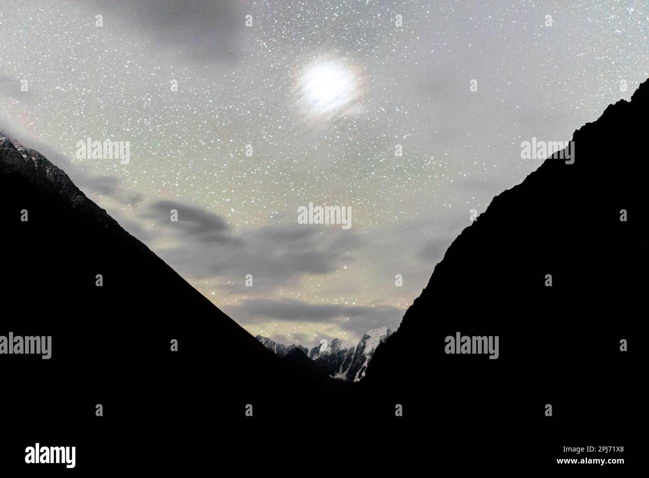 The moon with stars behind the clouds in the night sky illuminates the ...