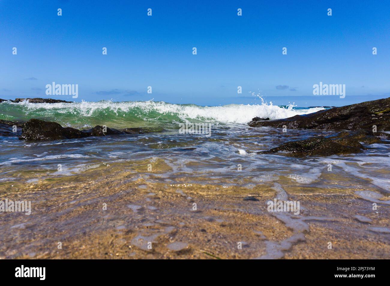 Low angle view of wave rolling in onto beach with clear blue sky above ...