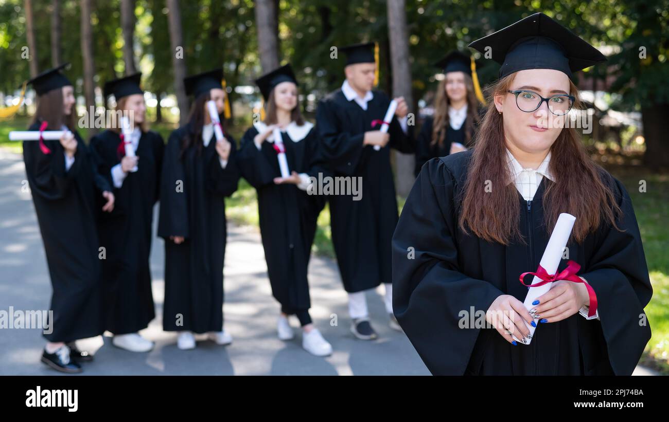 Portrait of a young caucasian woman in glasses and a graduate gown ...