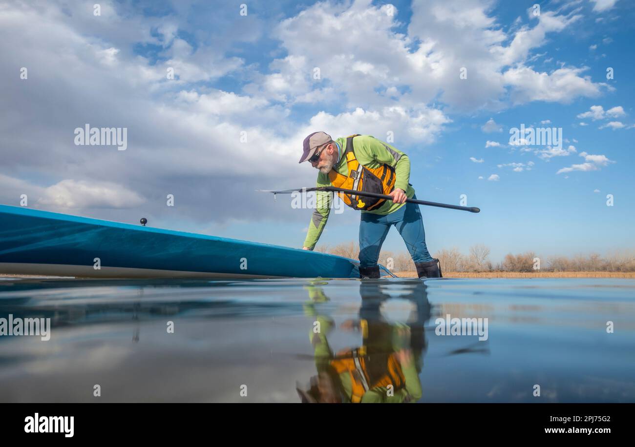 senior paddler and his paddleboard on lake in winter or early spring in ...