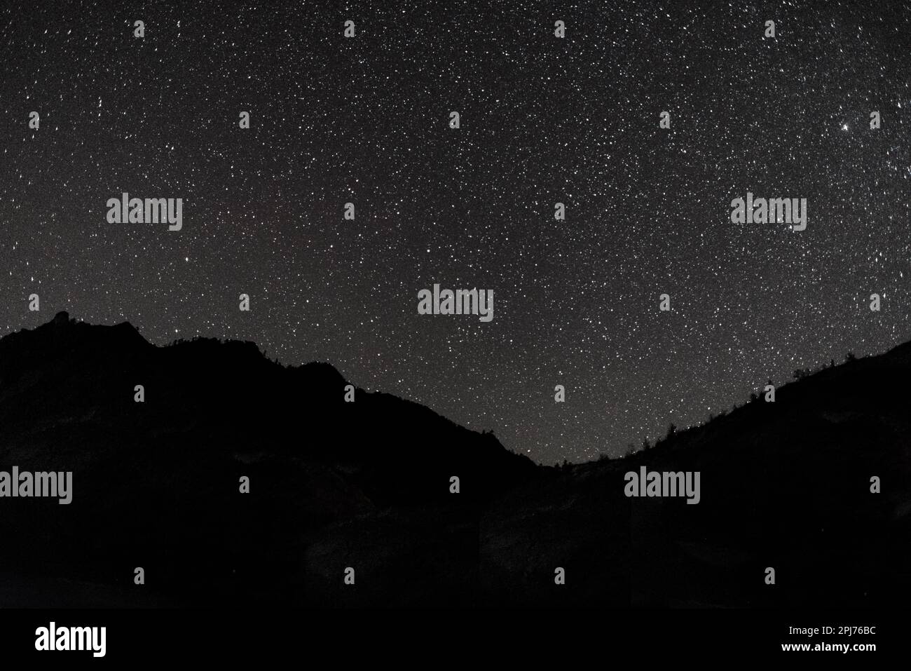 Black and white photo of a starry sky at night over a mountain and a ...