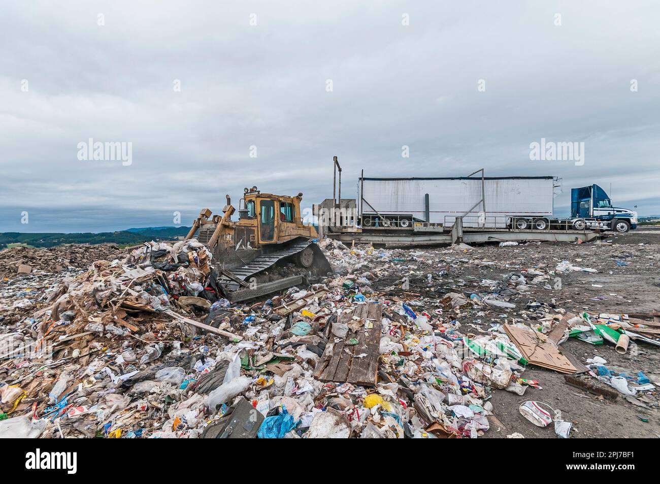 A soil compactor bulldozer pushing solid waste at an active landfill ...