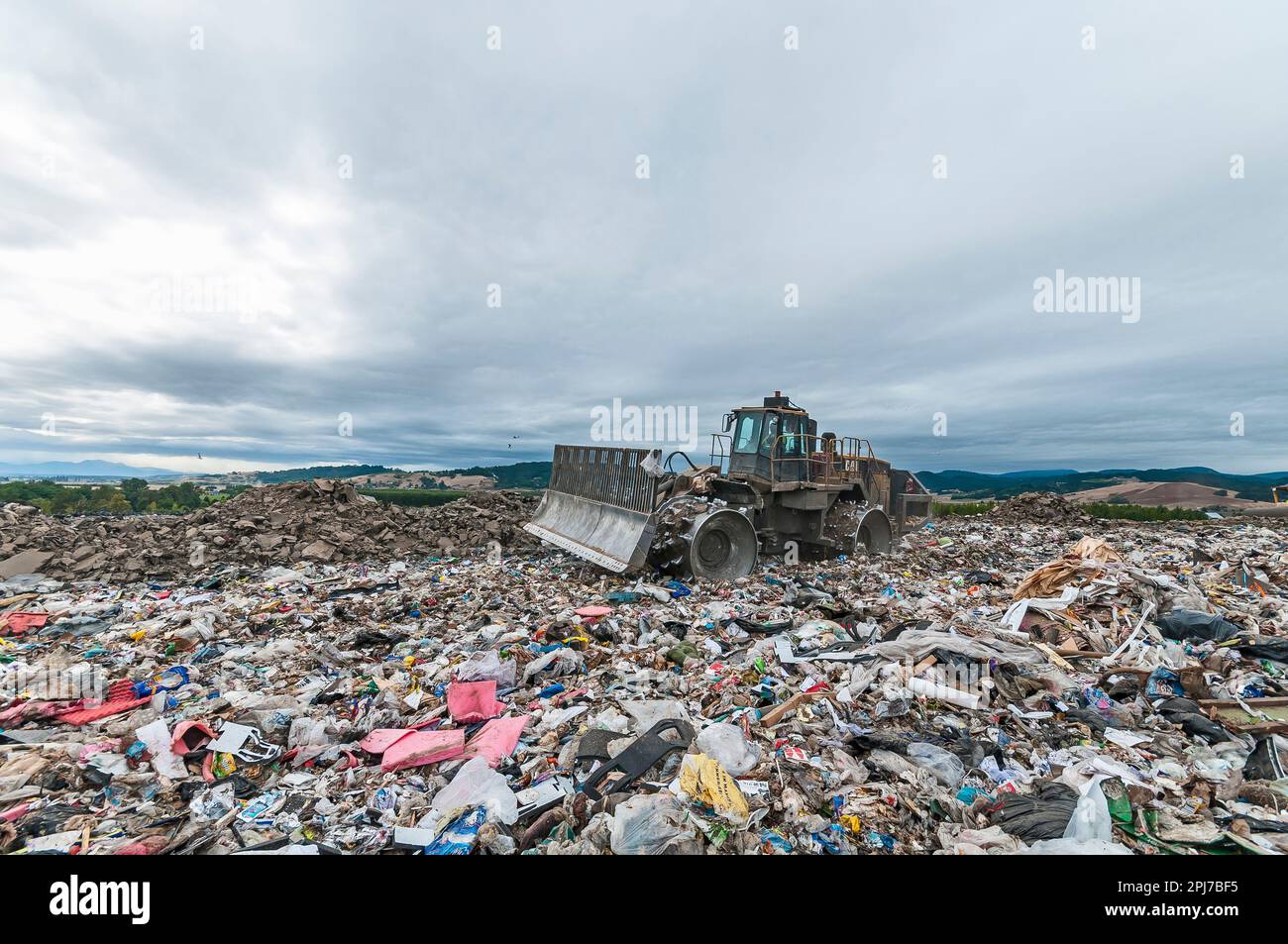 A soil compactor crushing solid waste at an active landfill Stock Photo ...