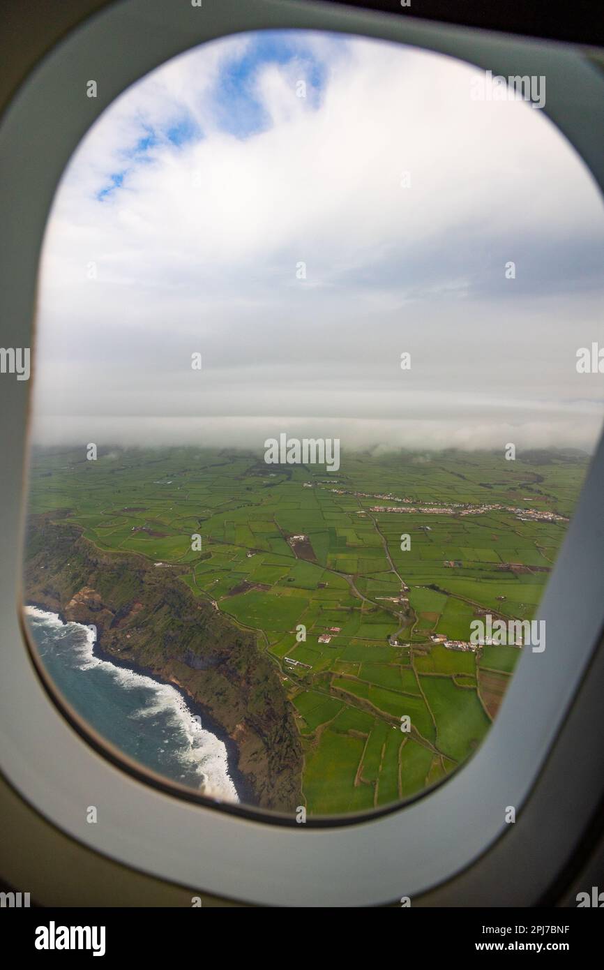 View to island from plane window, ocean, clouds and green fields Stock ...